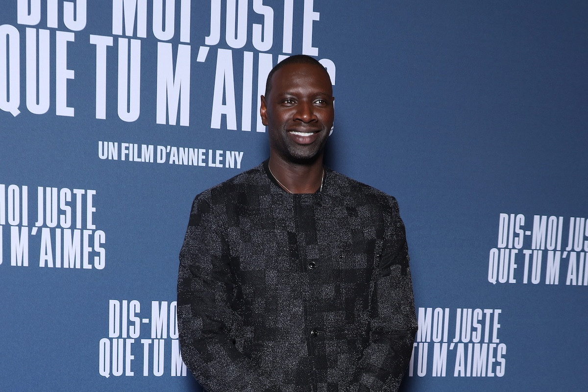 OMAR SY ATTENDS THE PREMIERE OF "DIS-MOI JUSTE QUE TU M'AIMES" WEARING JAEGER-LECOUTLRE